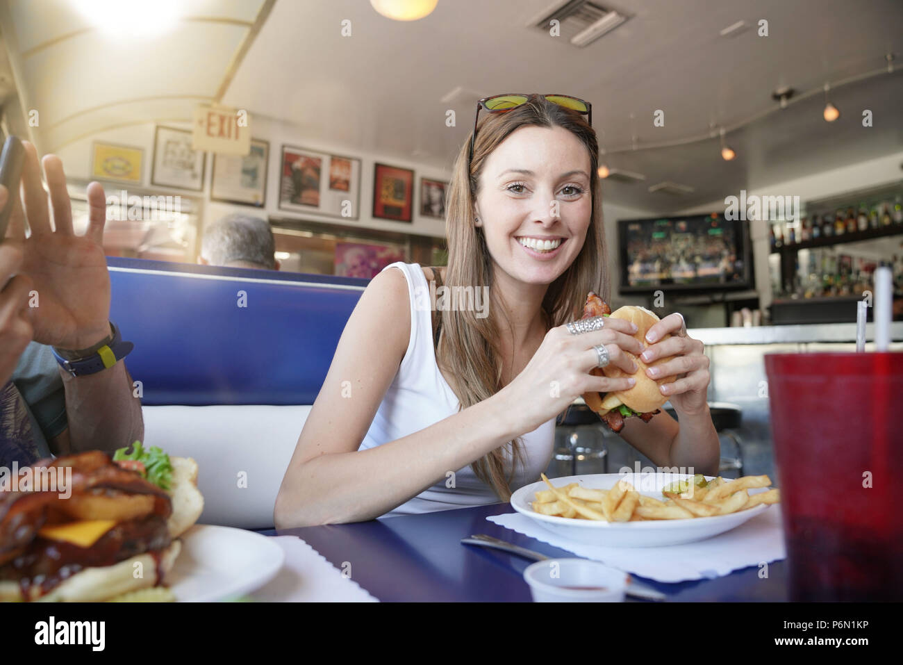 Portrait of cheerful girl eating hamburger in fast food restaurant ...