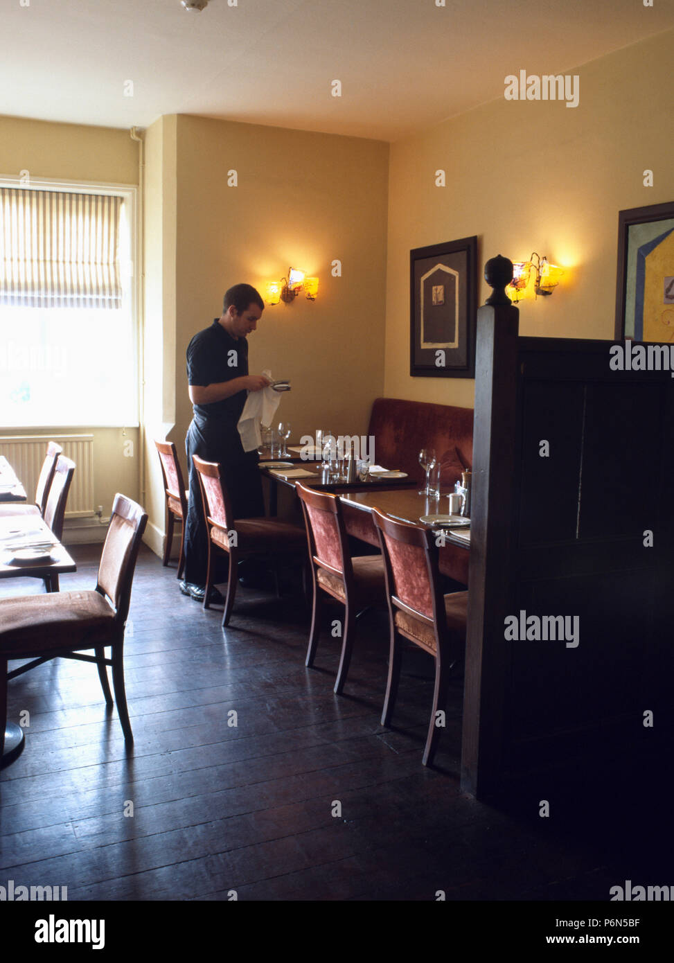 Waiter laying up tables in traditional restaurant with wooden flooring ...