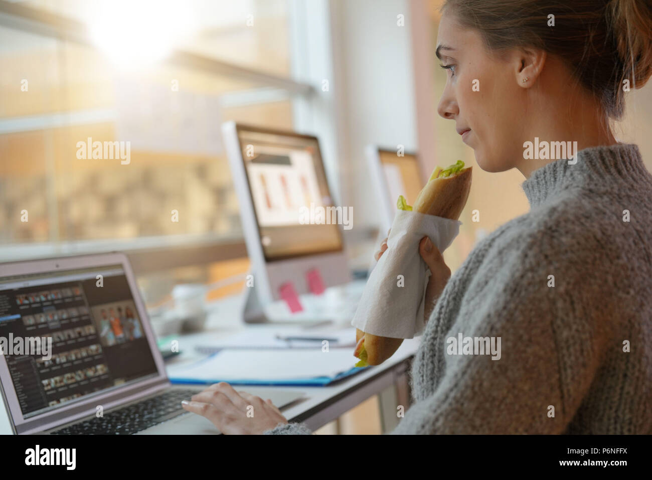 Young woman student eating sandwich in front of laptop computer Stock ...