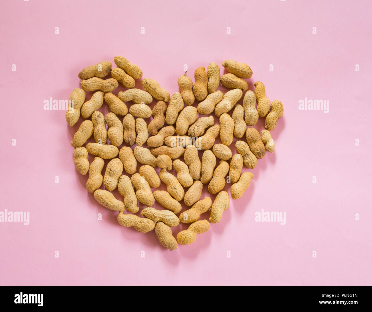 Peanuts forming a heart on pink background Stock Photo - Alamy