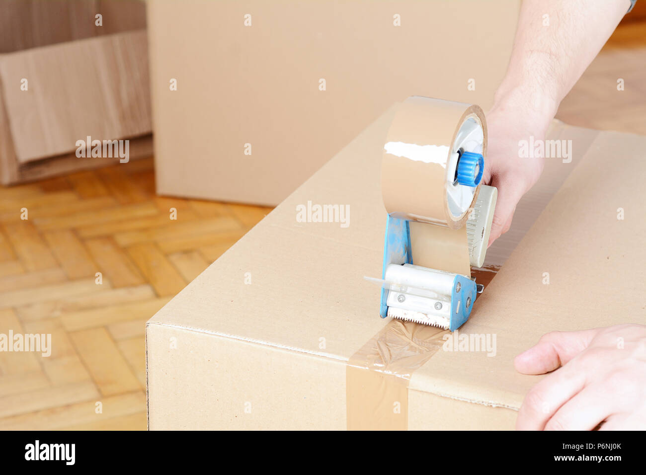 Man sealing a shipping cardboard box with tape dispenser. Indoors Stock ...