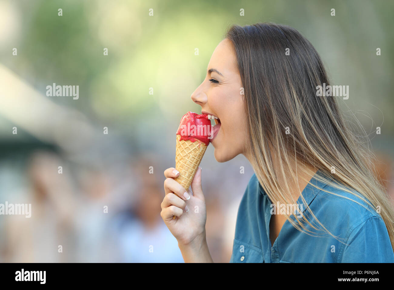 Side view portrait of a happy woman biting an ice cream on the street ...