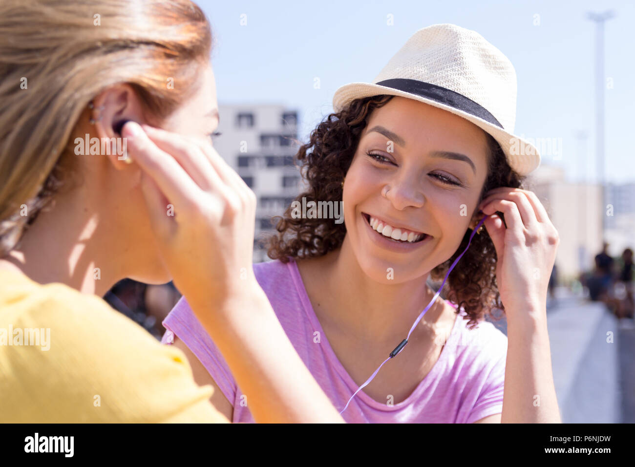 Two young friends with bright color clothing and hat listening to music ...