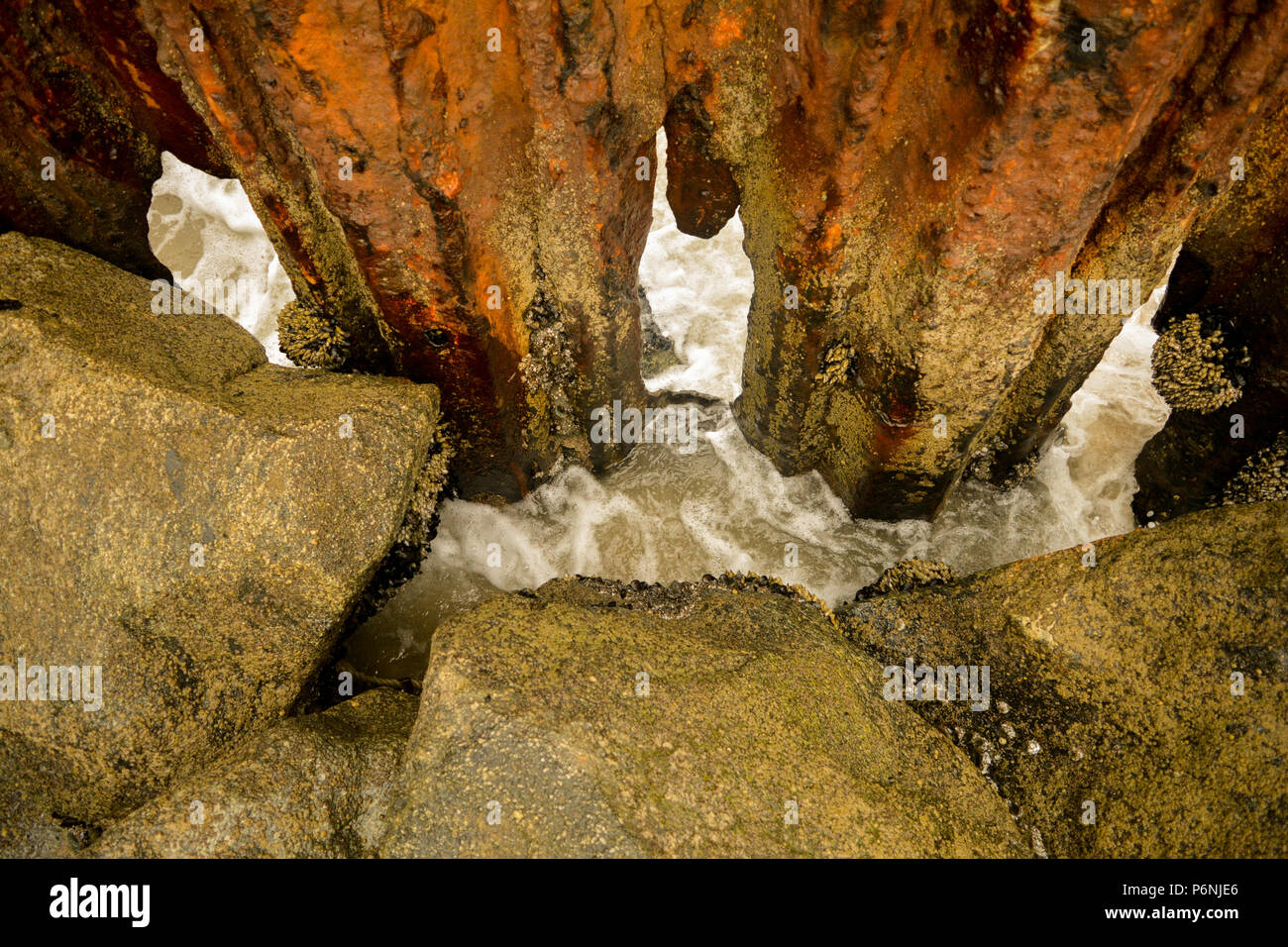 Big rocks and rusty metal in water by beach with sand and rough water ...