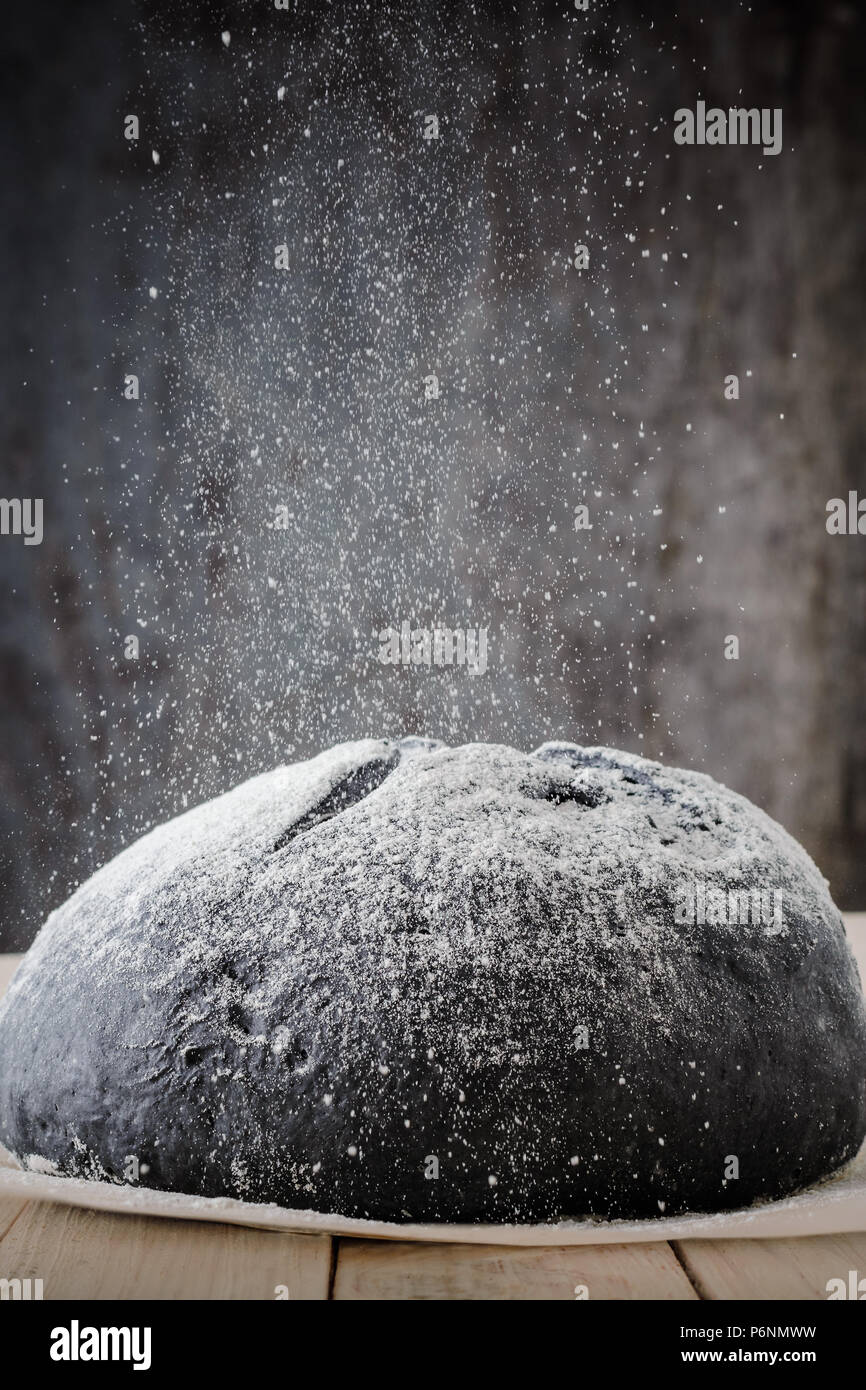 Round rye bread of black color is sprinkled with flour. Dark background ...