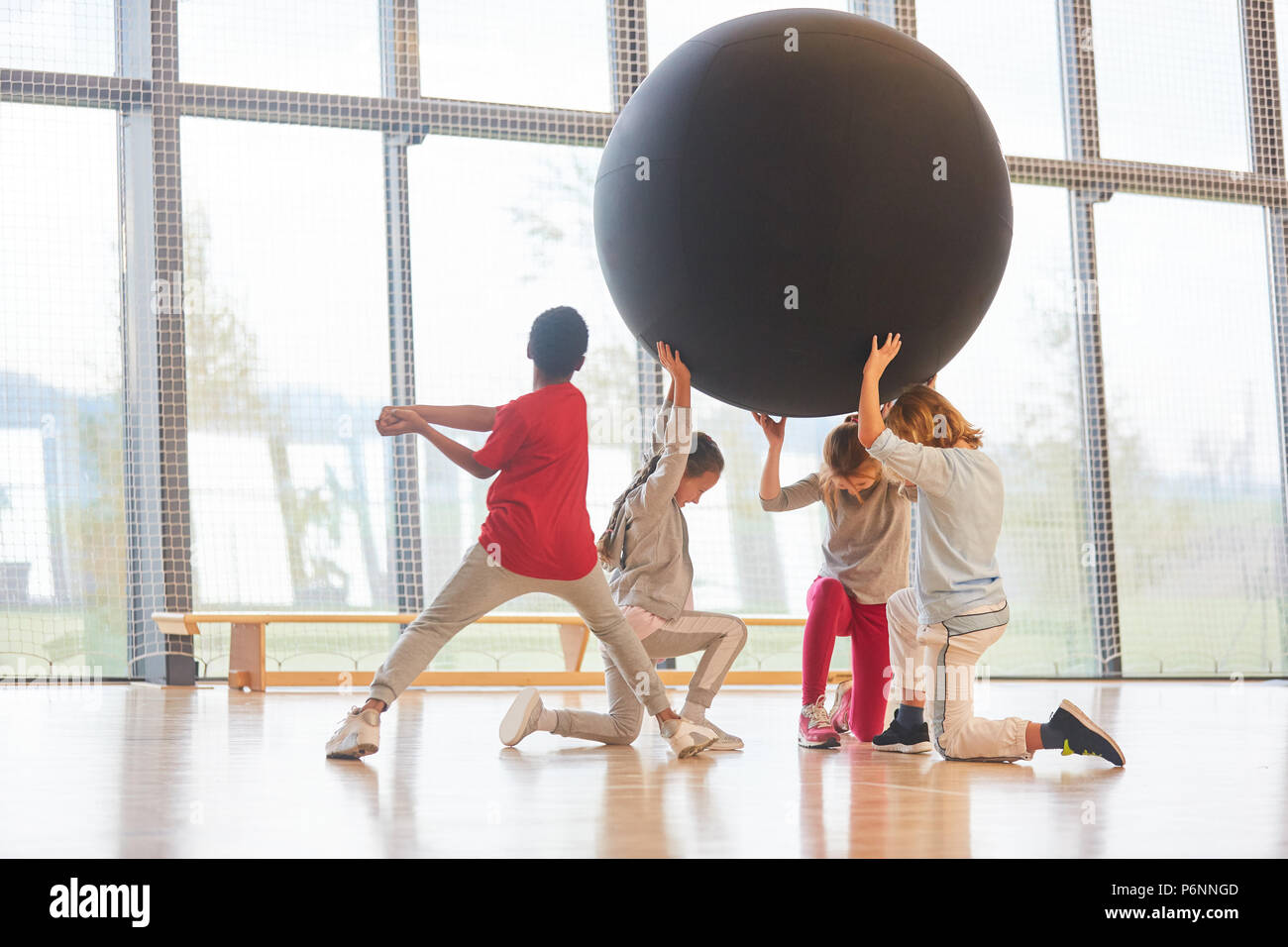 Sporty pupils raise a huge ball in the gym in teamwork Stock Photo - Alamy