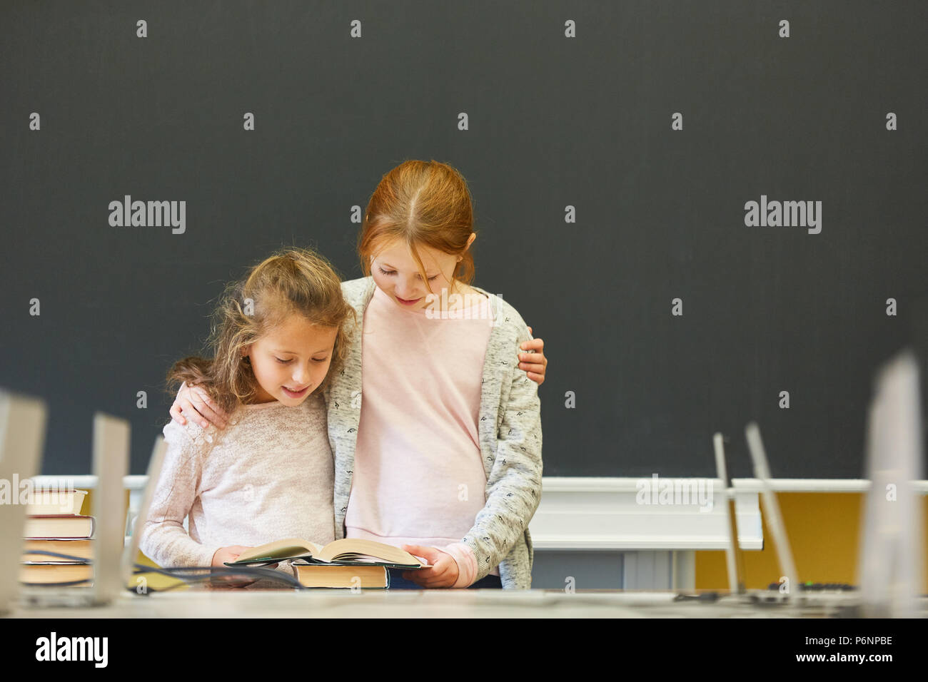Two girls as elementary school students learn to read together in the ...