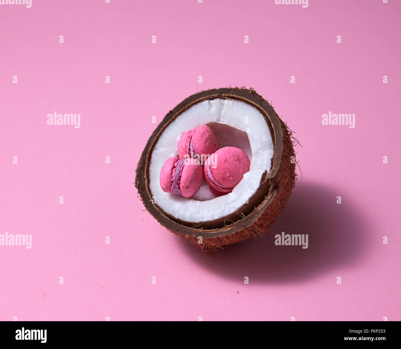 Coconut halves with pink mini macaroons on pastel pink background ...