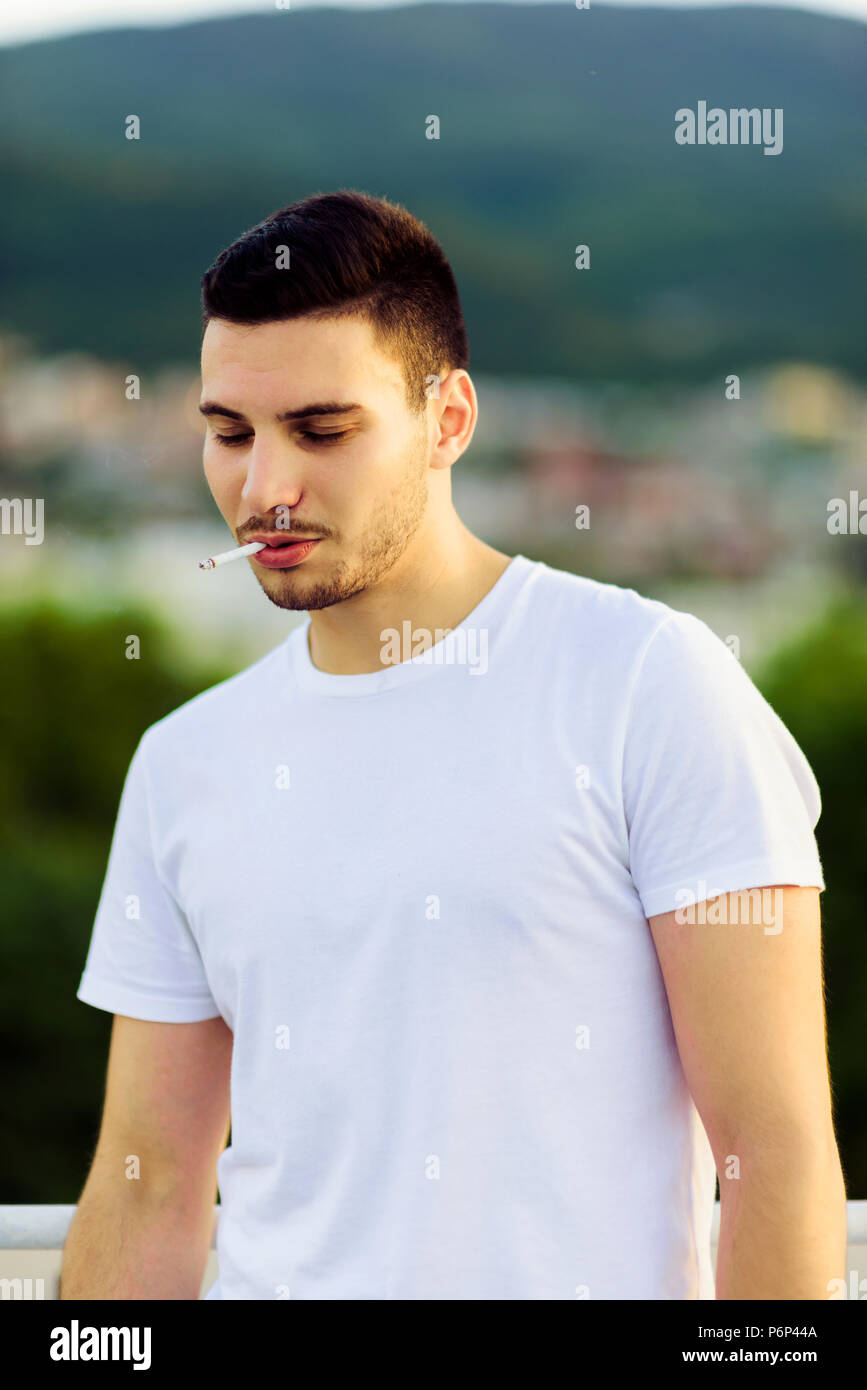 Picture of a handsome young man smoking a cigarette on the terrace ...