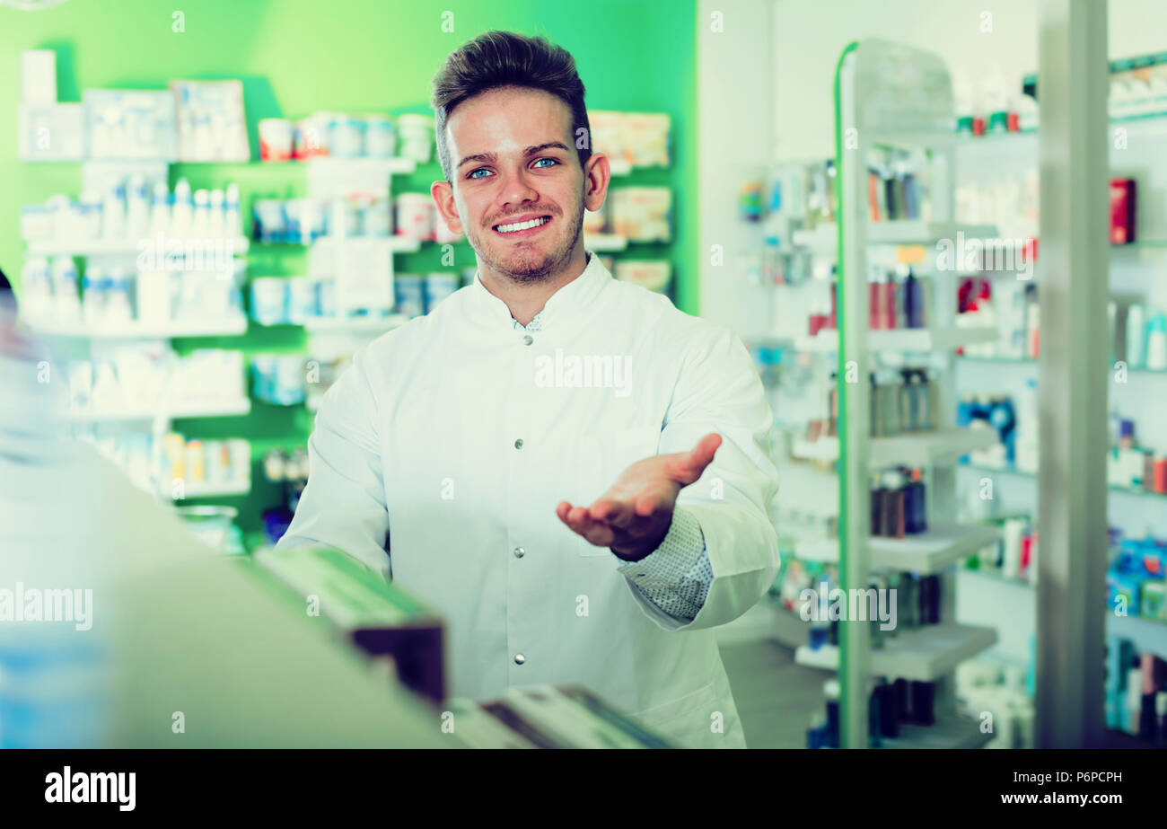 Laughing pharmacist wearing white coat standing among shelves in drug ...