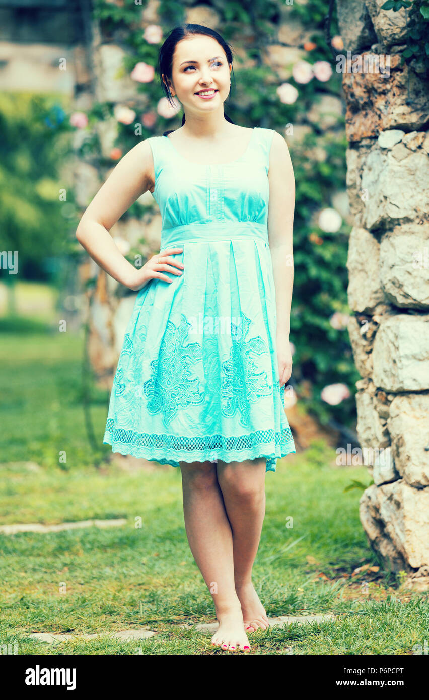 portrait of young smiling germany woman in dress near roses in a garden ...