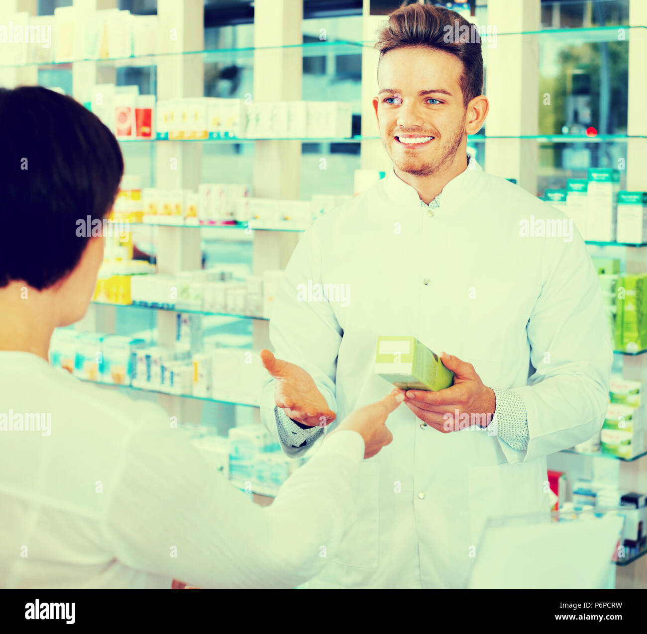 Cheerful positive man pharmacist wearing uniform assisting customers in ...