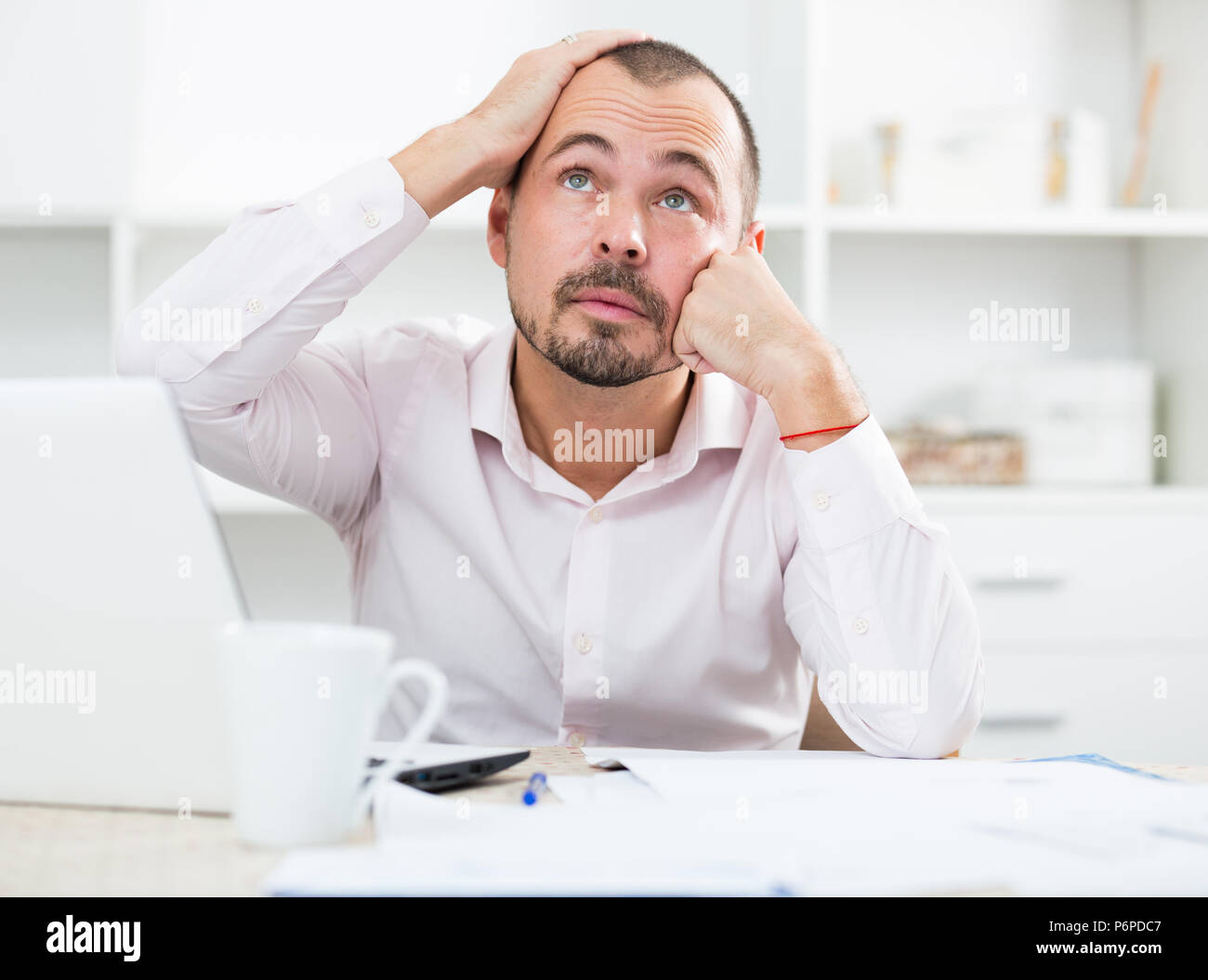 Disappointed worker at his office table feeling stressed, thinking and ...