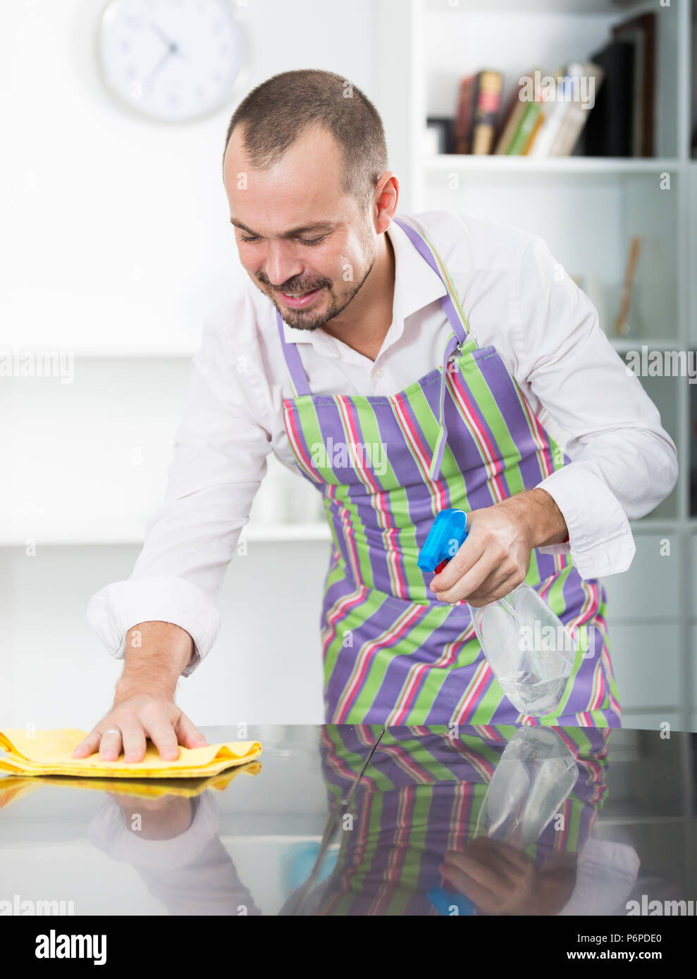 Positive young man in apron cleaning his office desk by cleanser Stock ...