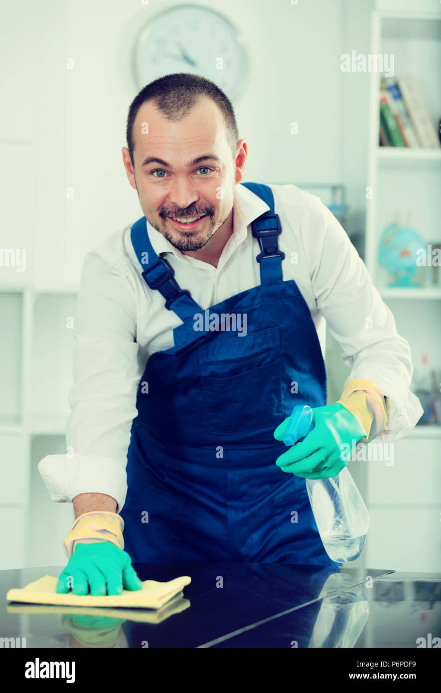 Positive young man in apron cleaning his office desk by cleanser Stock ...
