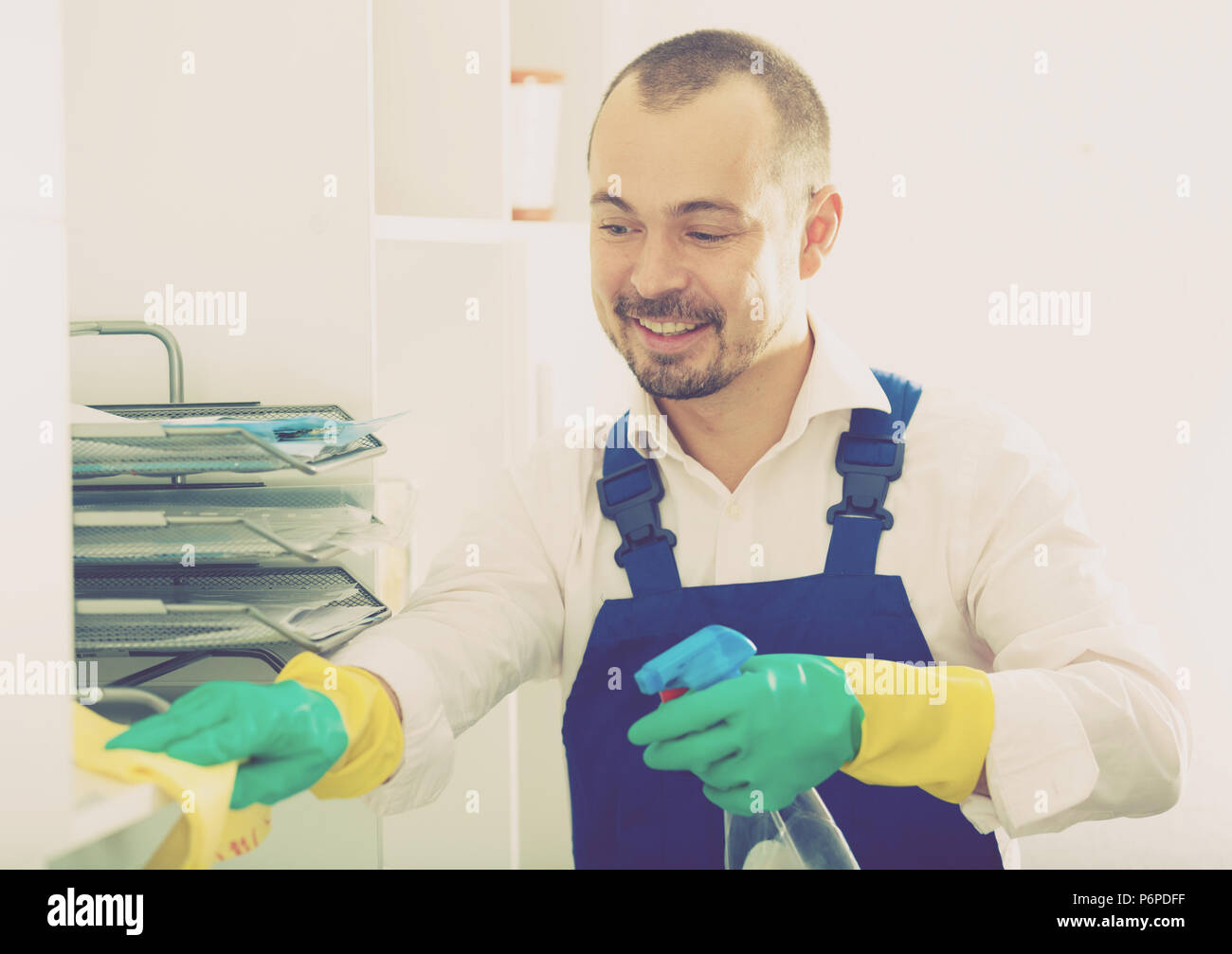 Young happy european businessman in office dusting surfaces in latex ...