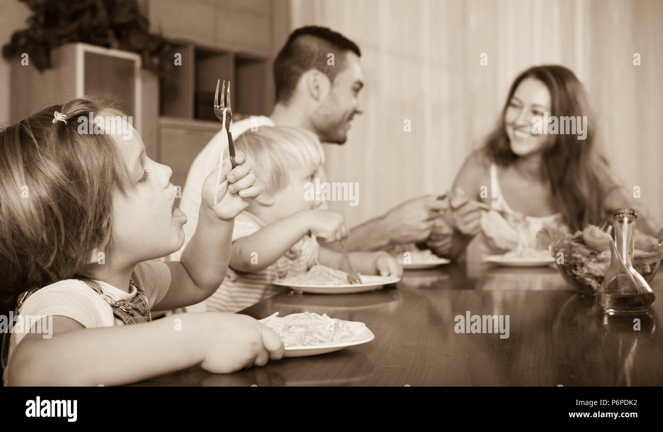 Positive young family of four eating with spaghetti at table. Focus on ...