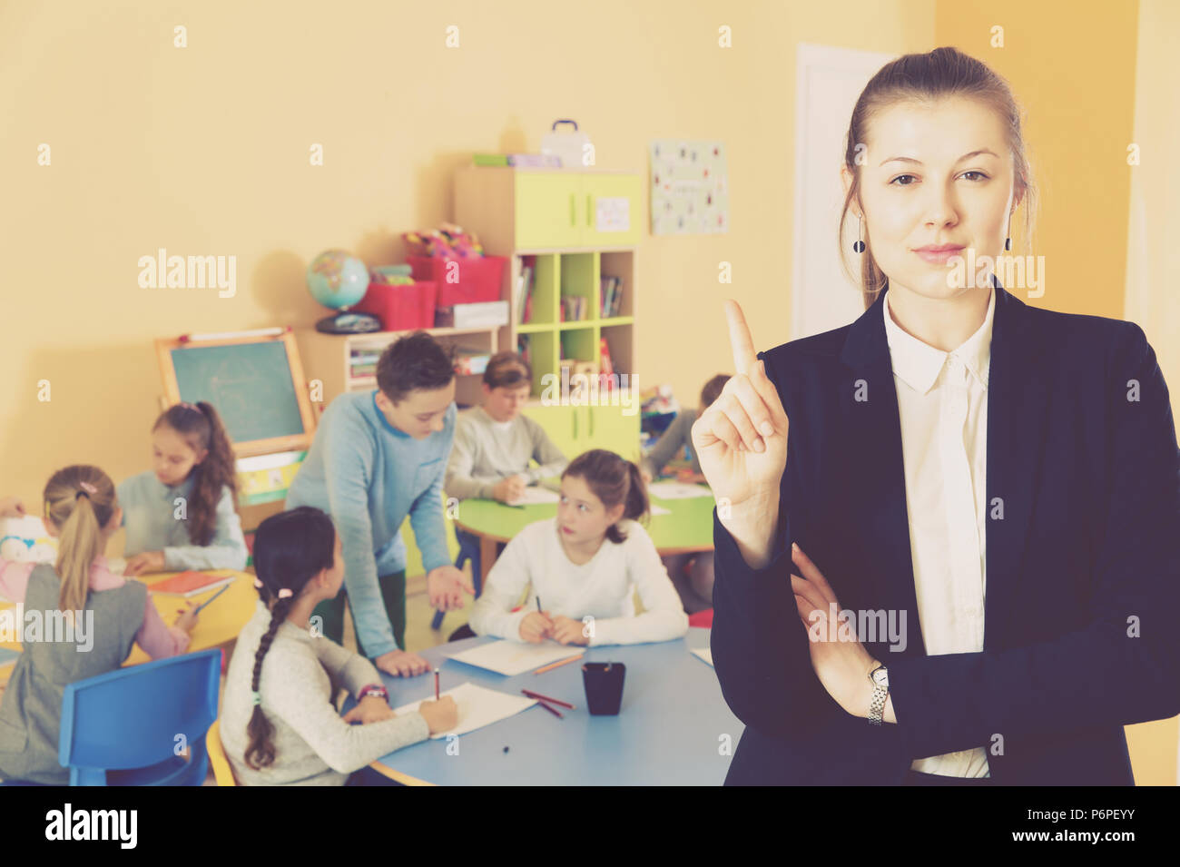 Strict pleasant female teacher standing foreground in classroom with ...