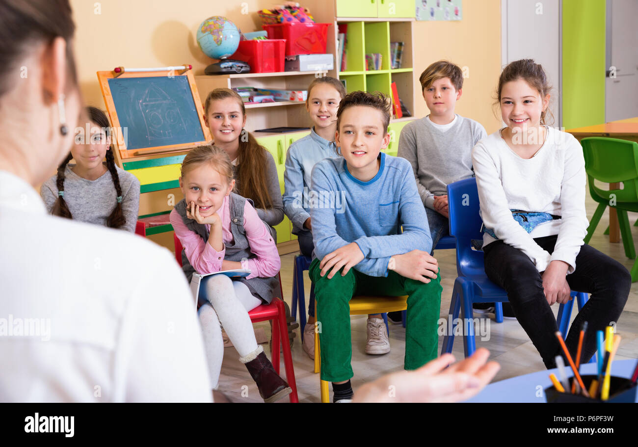 Portrait of friendly smiling positive pupils listening teacher at ...