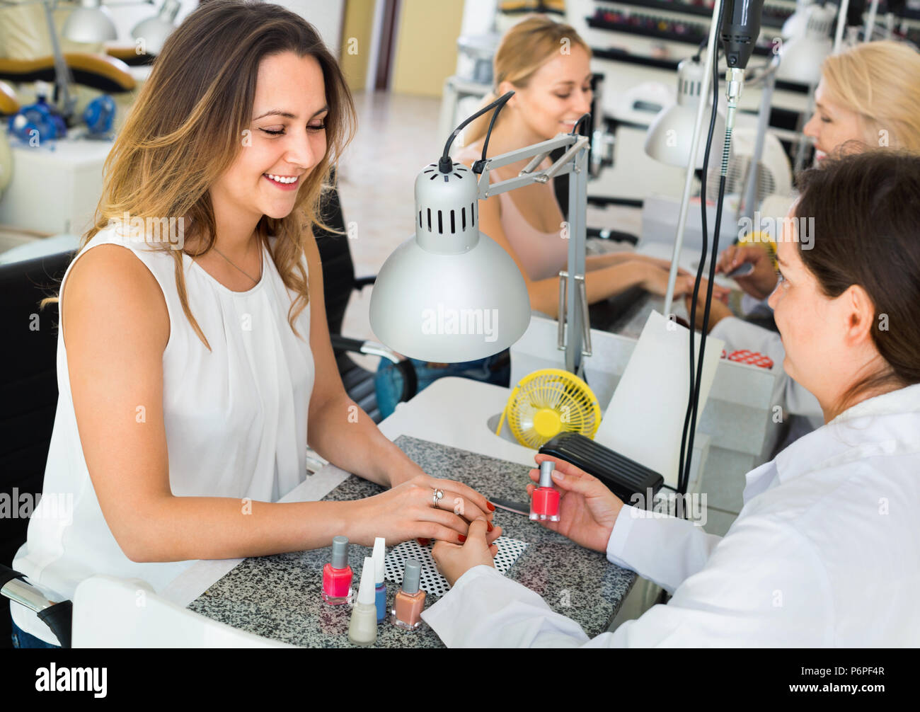 Two happy positive women clients having manicure done in nail salon ...