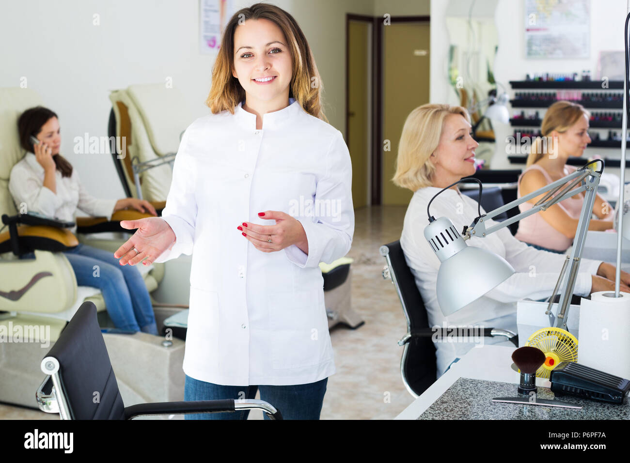 Pretty young girl doing nails displaying her workplace in nail salon ...