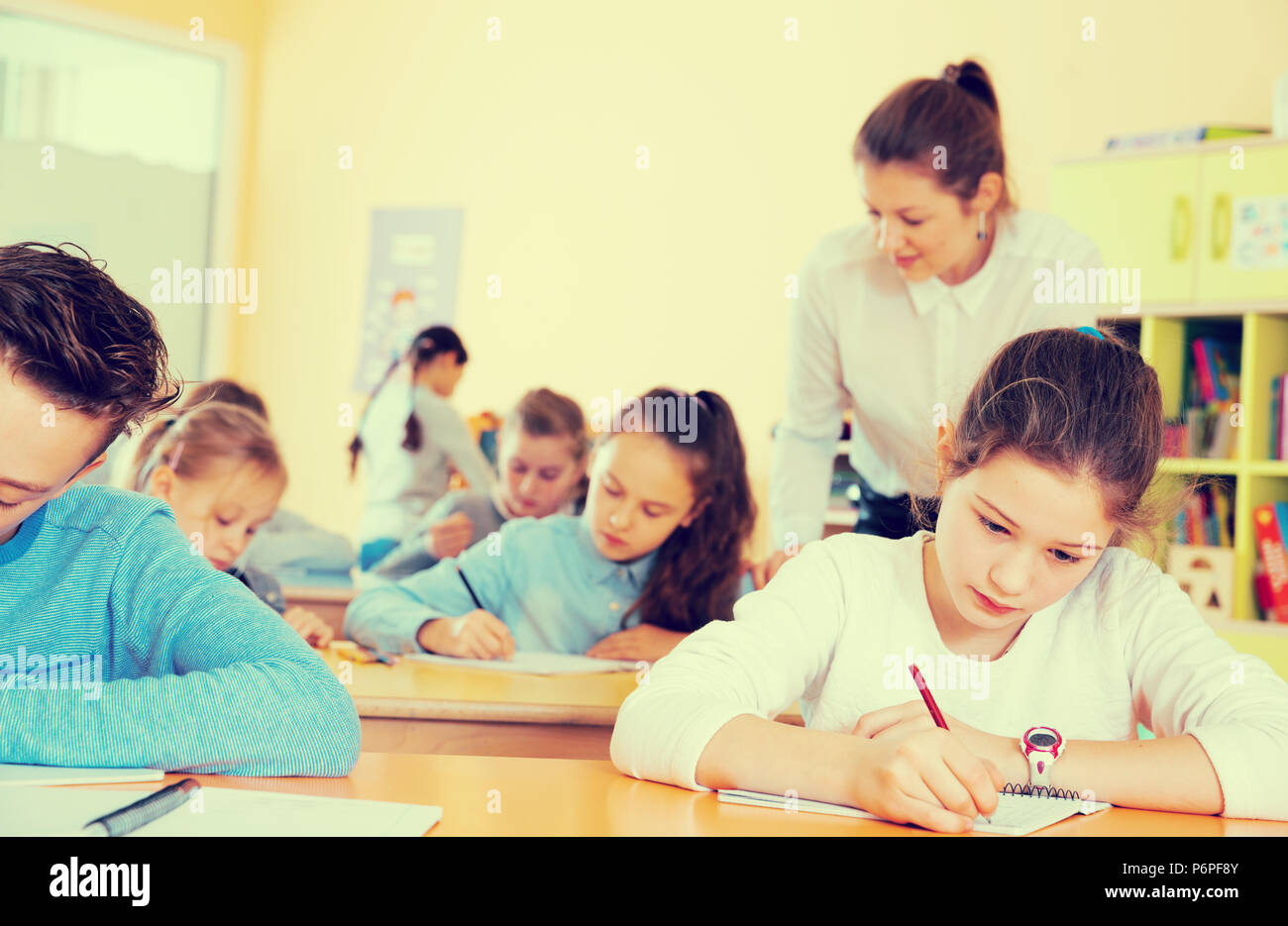 Group of school kids with pens and notebooks studying in classroom with ...
