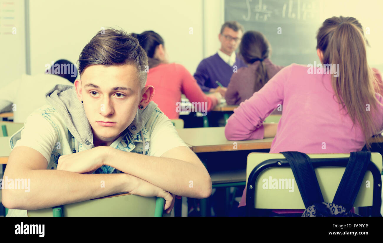 lonely school boy sitting away from classmates and feeling depressed ...