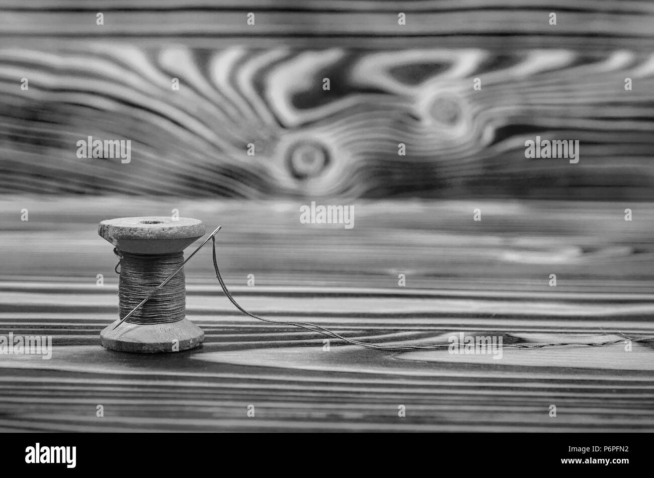 The old reel of thread and a needle on a wooden table in black and ...