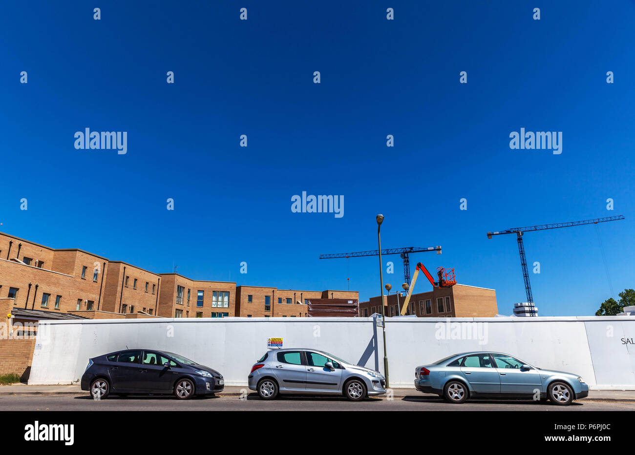 Three cars parked outside a construction site with two tower cranes in ...