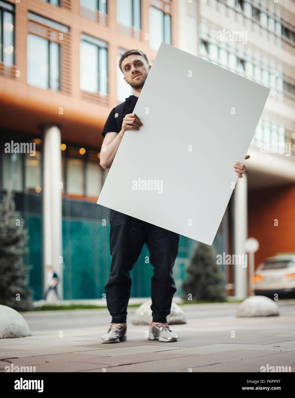 Attractive man holding blank canvas at the street and looking at the ...