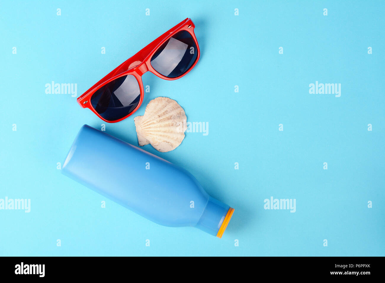 Top view of sunglasses, shells and sunblock on Light blue background ...