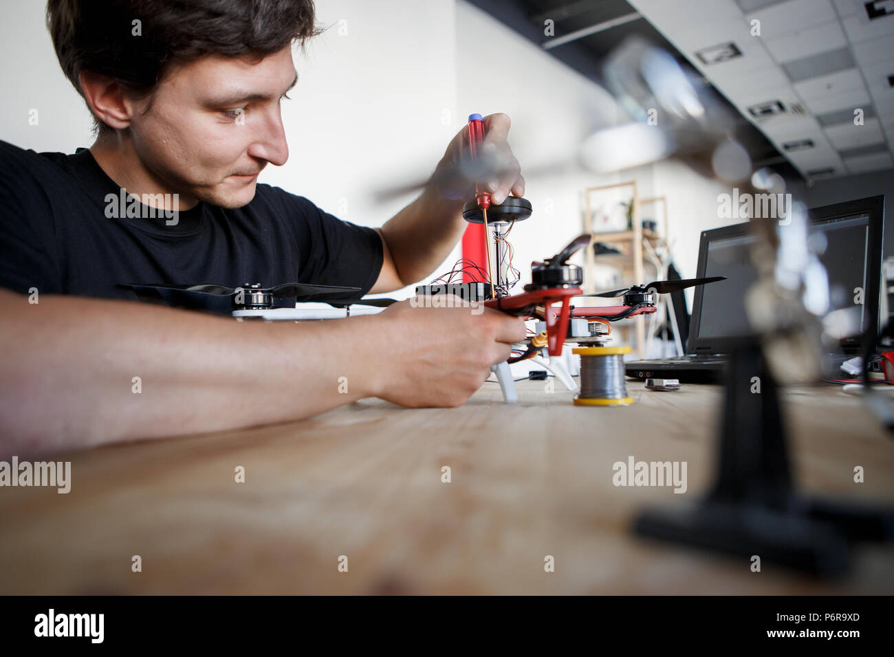 Image of man with screwdriver fixing square copter at table Stock Photo ...