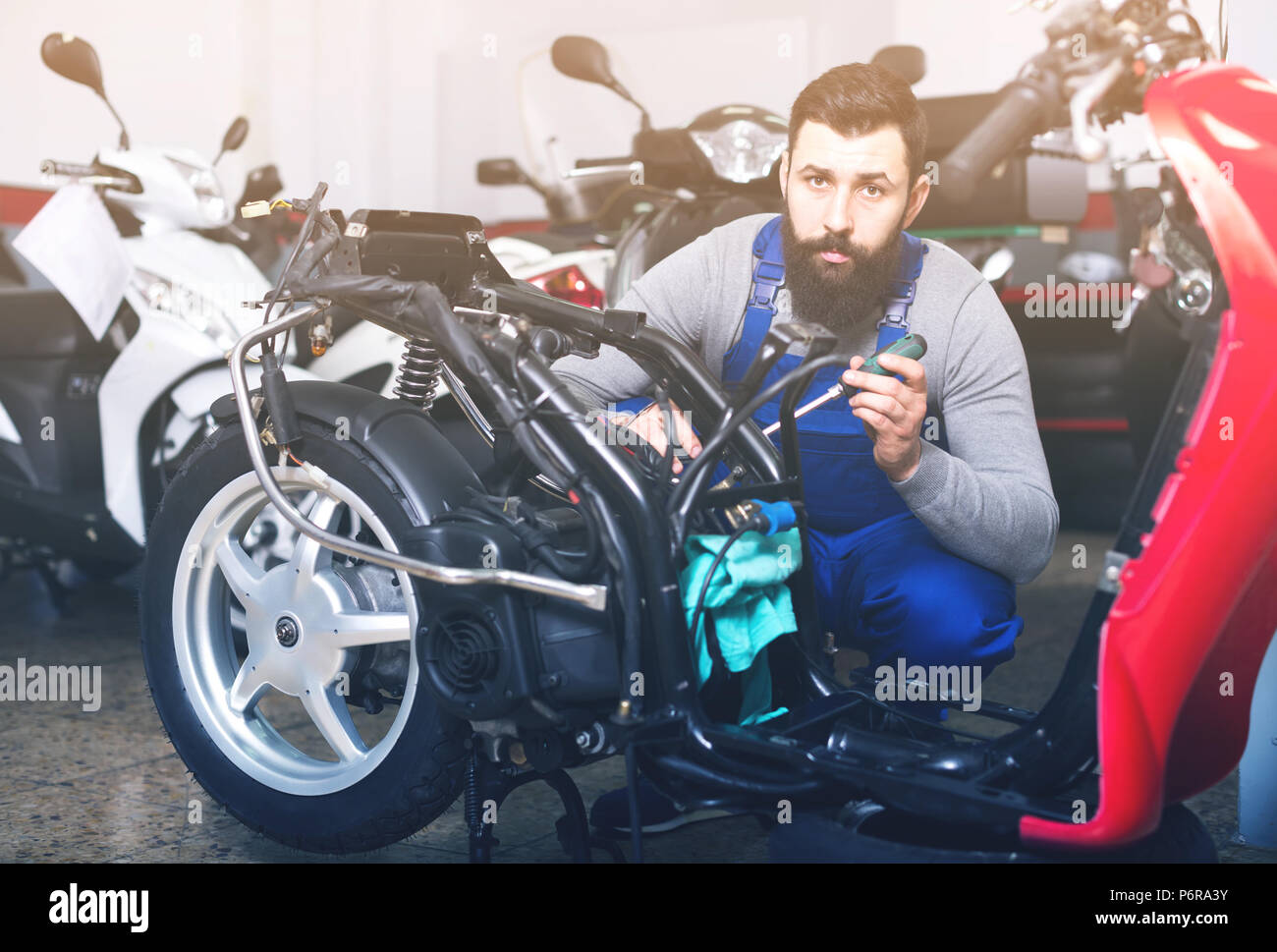 Young male worker working at restoring motorbike in motorcycle workshop ...