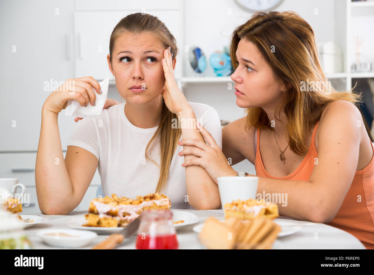 Female talking with young sad friend at the table with cake at home ...