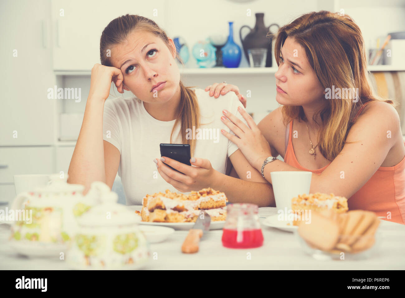 Portrait of female talking with sad girl friend with mobile at the ...