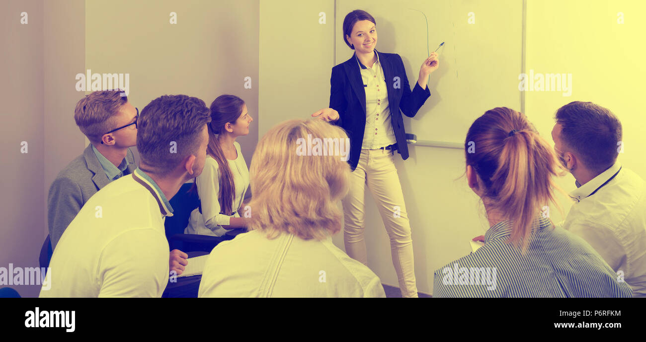 Group of smiling students attentively listening to lecture of female ...