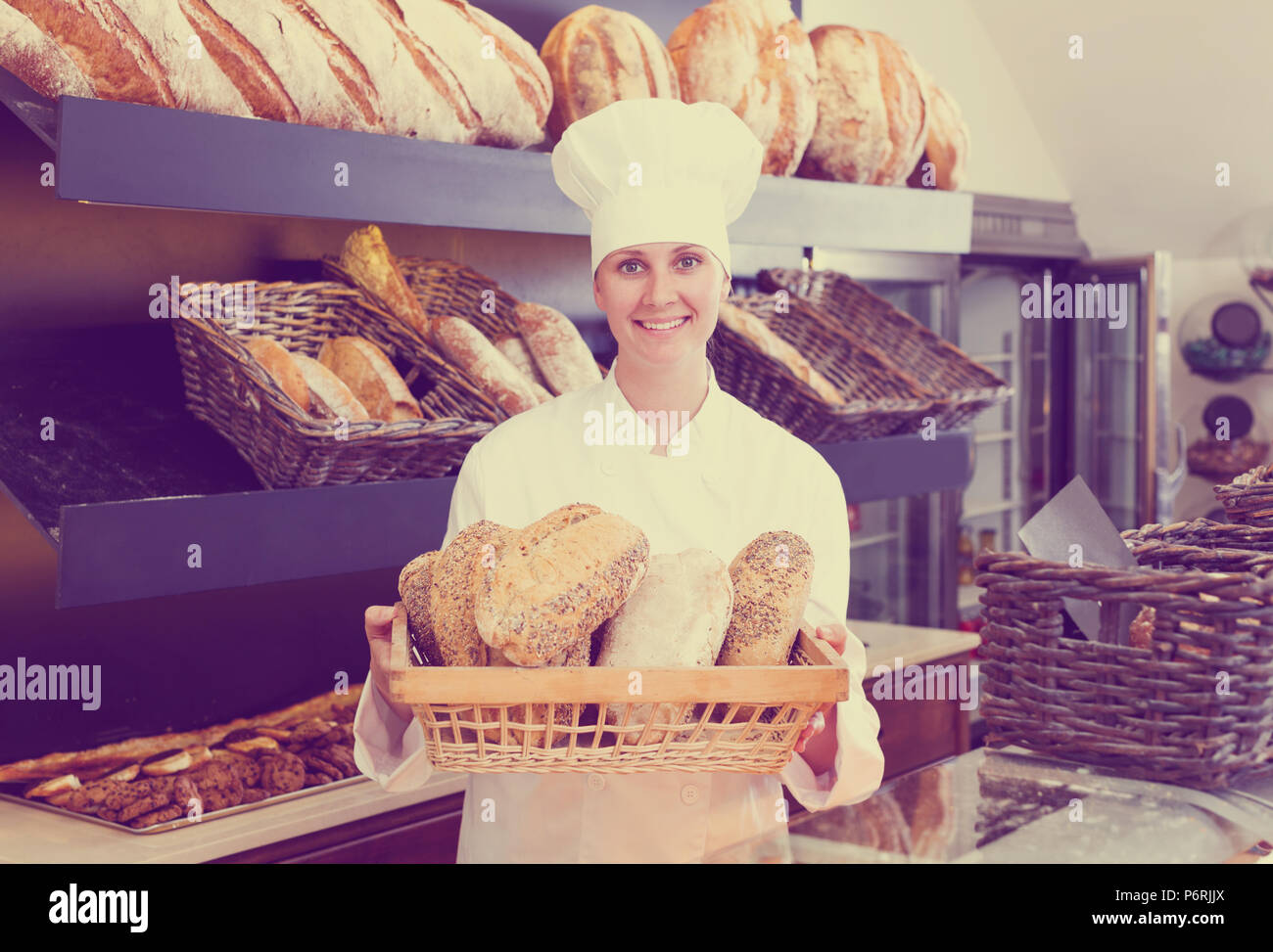 Happy bakery female employee with tasty and fresh bread products on ...