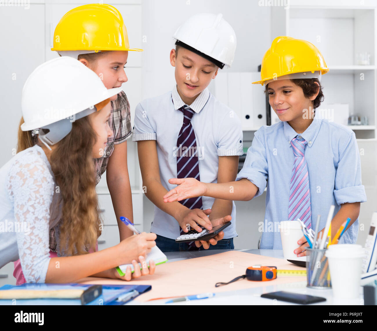 Teens in color helmet engineers discussing draft at the table Stock ...