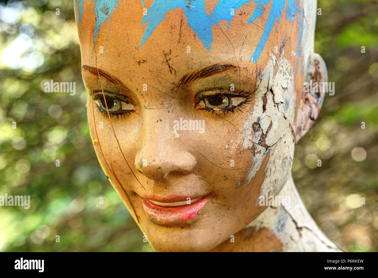 A damaged, painted, abandoned mannequin stands outdoors in a forest ...