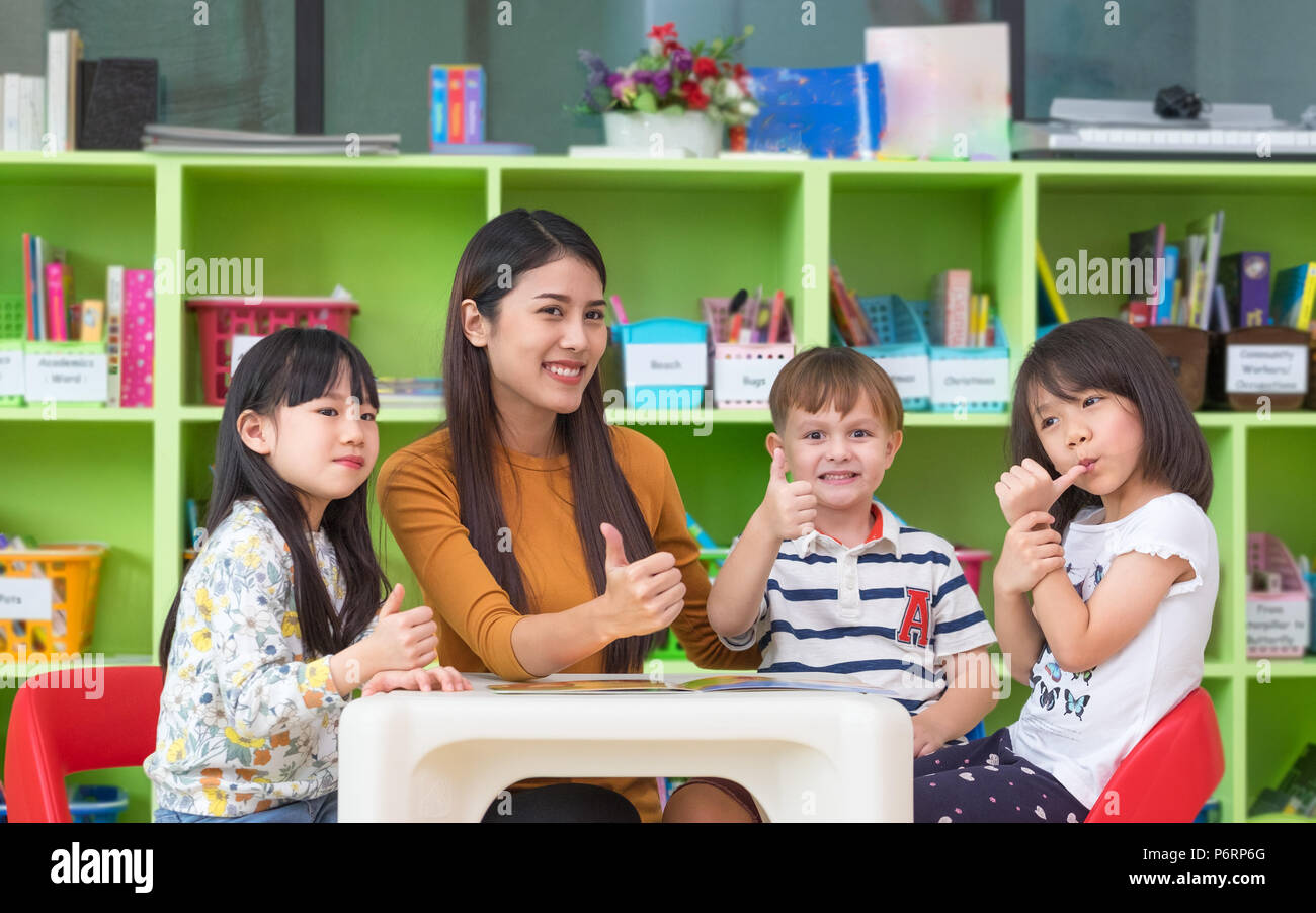 Asian female teacher and mixed race kids thumbs up in classroom ...