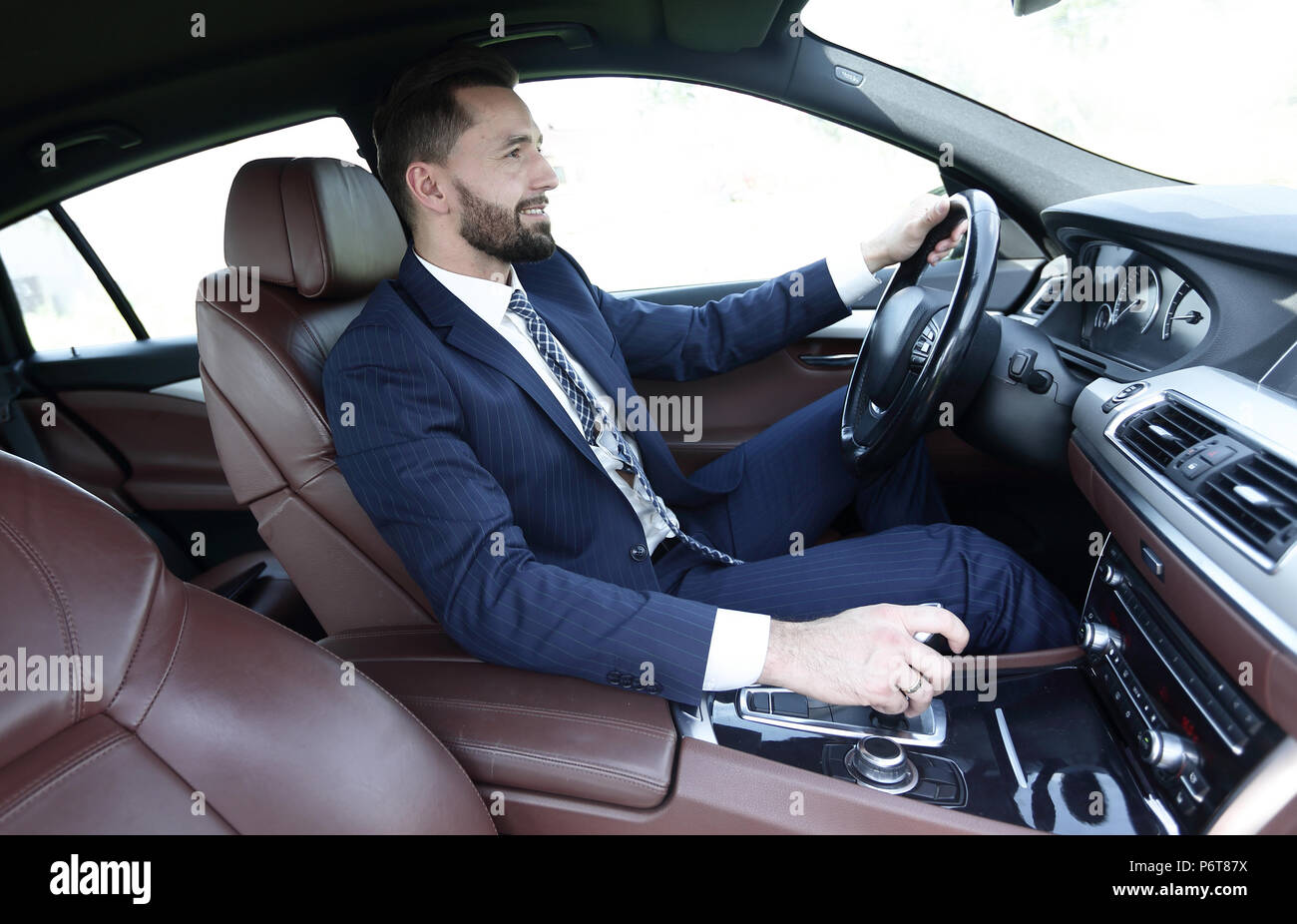 View from the side confident businessman sits at the wheel of a car ...