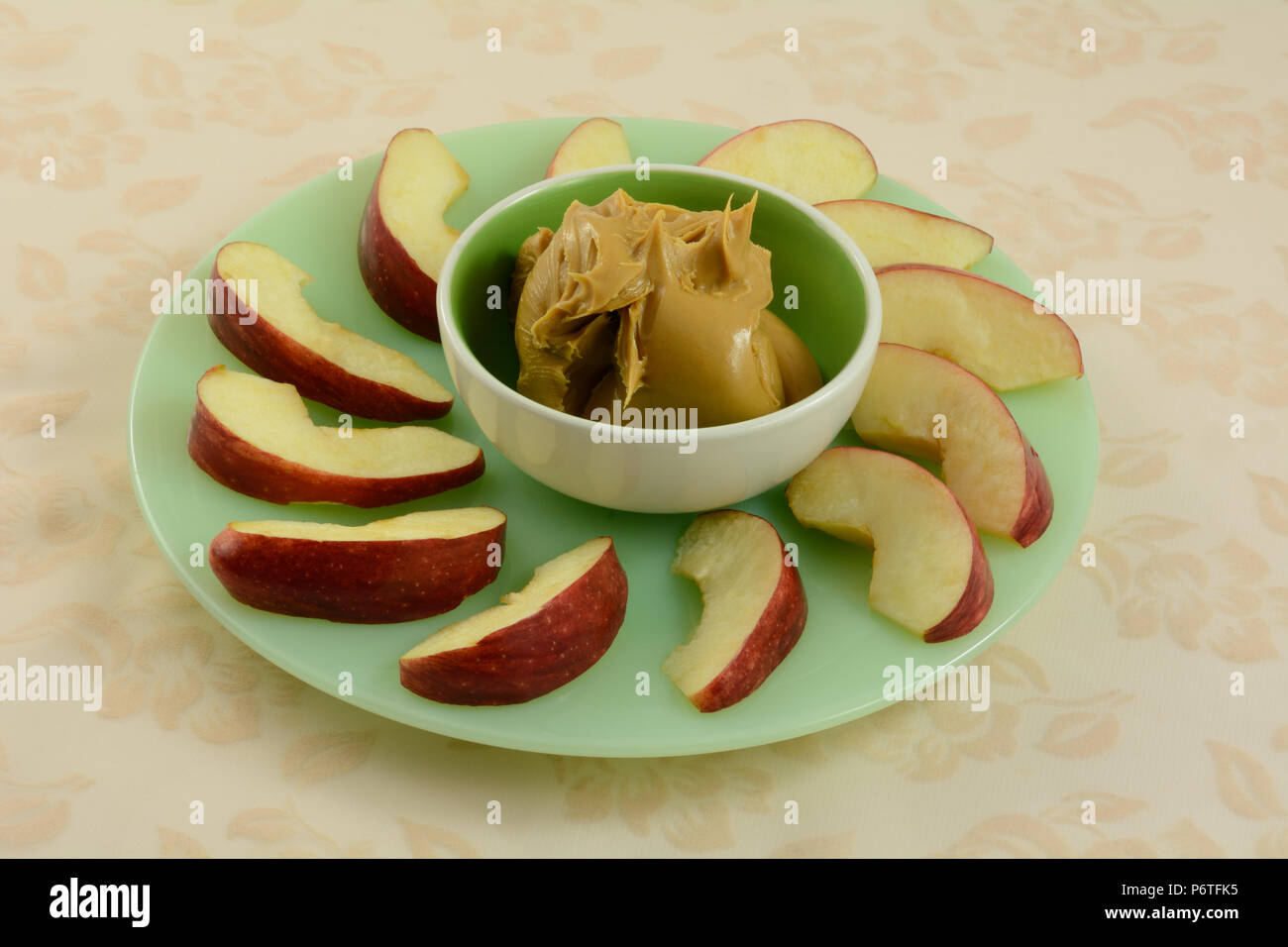 Apple slices on green snack plate with small green bowl full of peanut ...