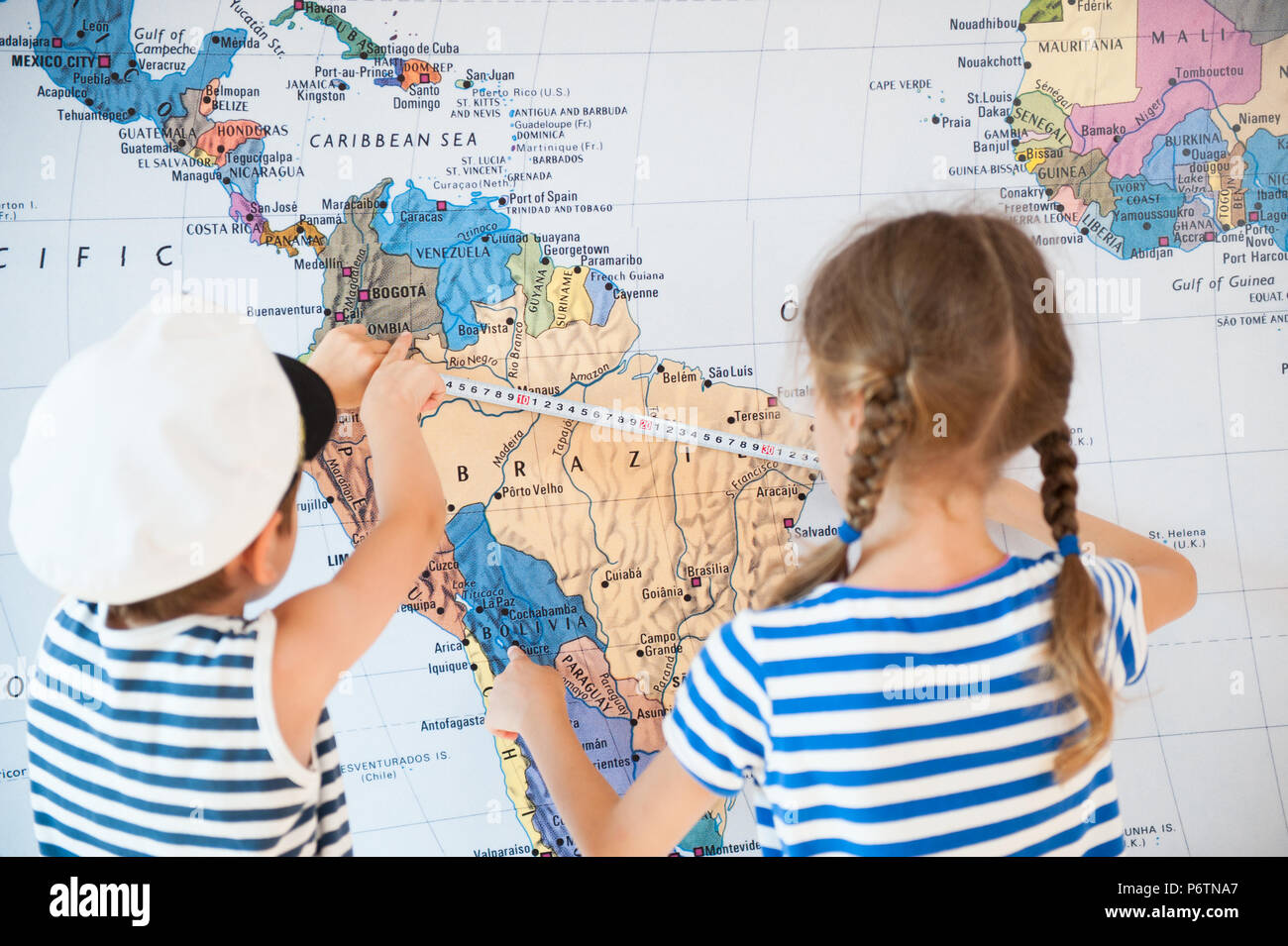 little boy in captain hat and girl in striped shirt studying world map ...