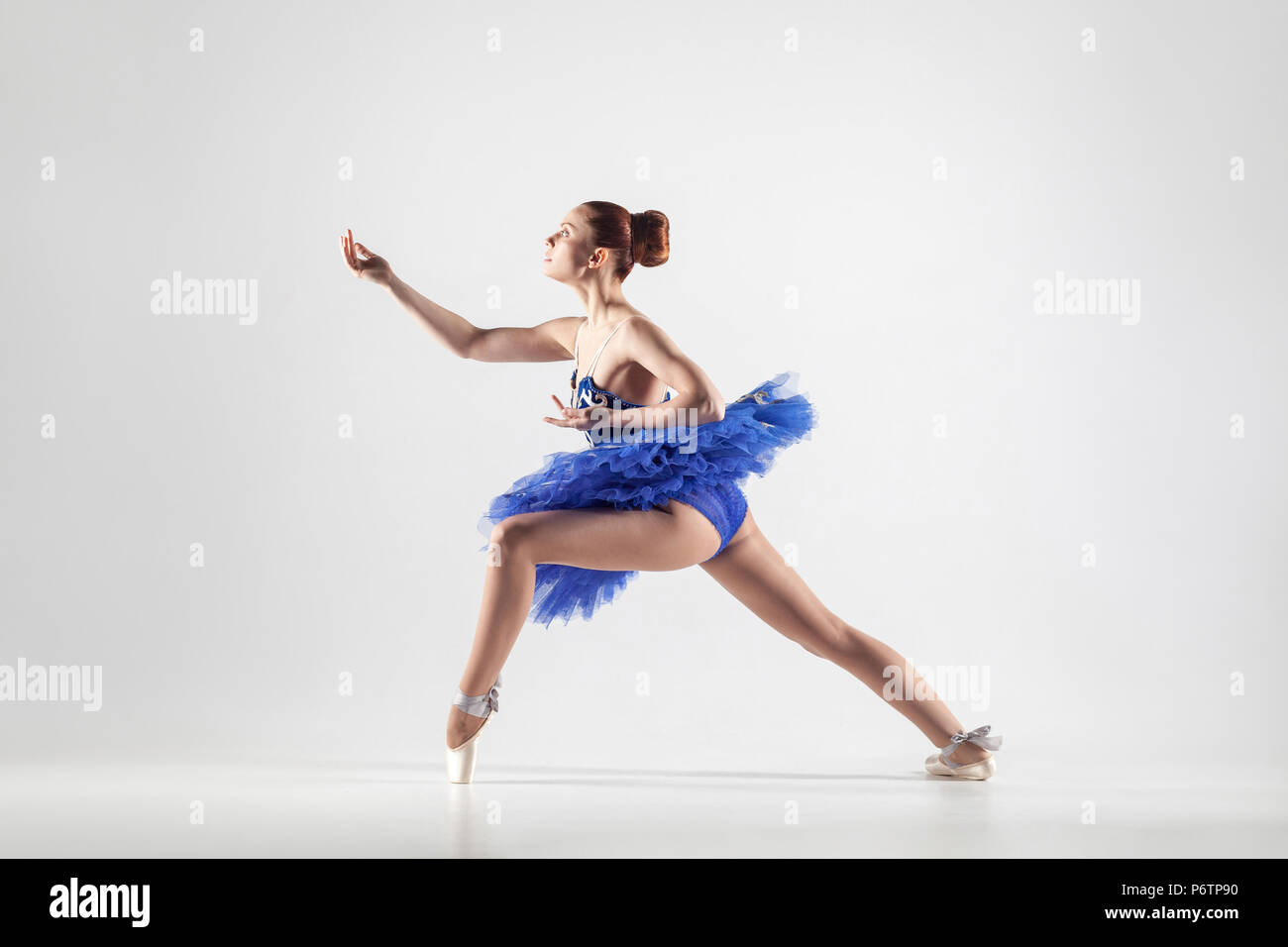 Young beautiful ballerina with bun collected hair wearing blue dress ...