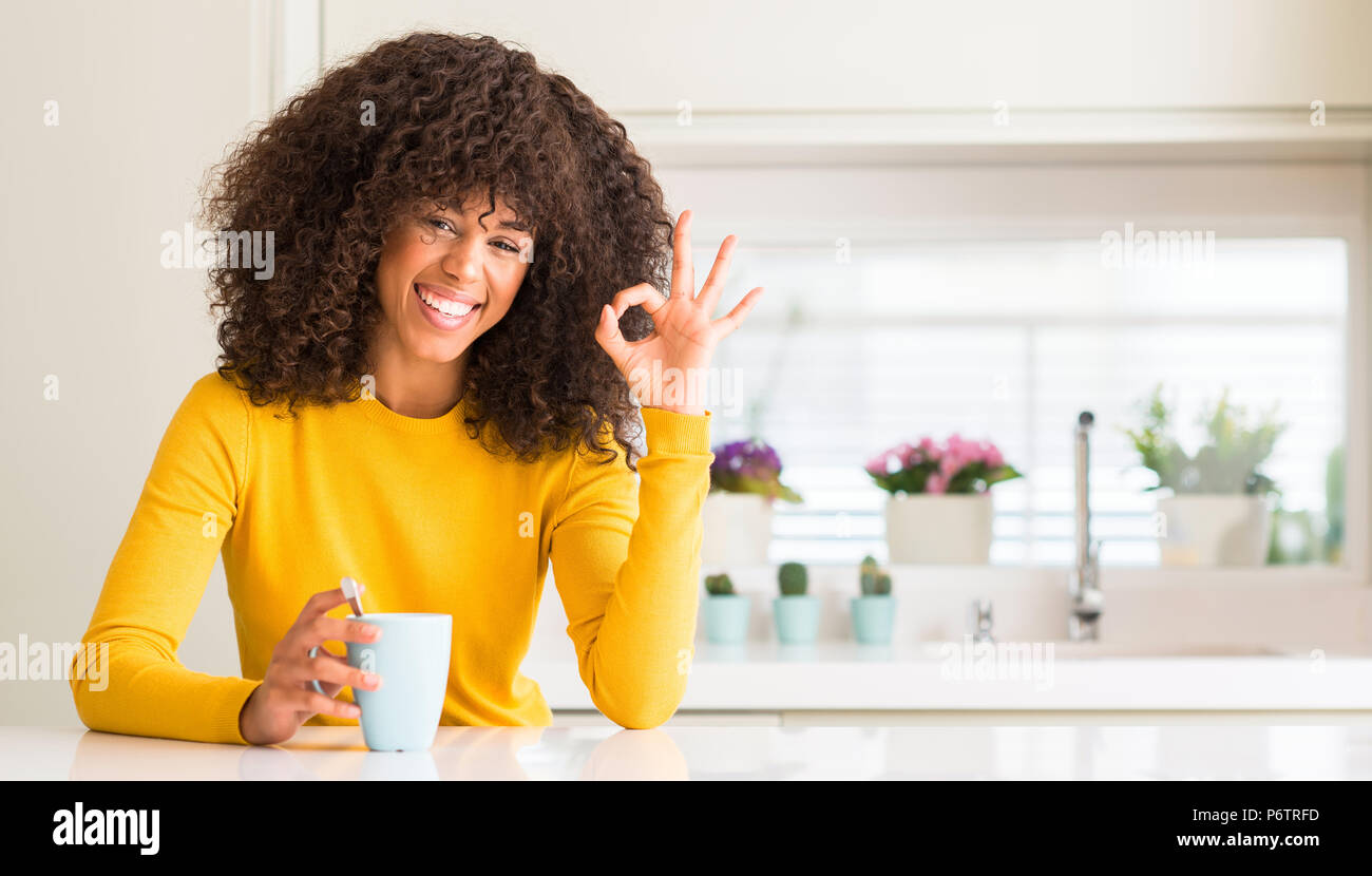 Beautiful african american woman holding a cup of coffee at home doing ...