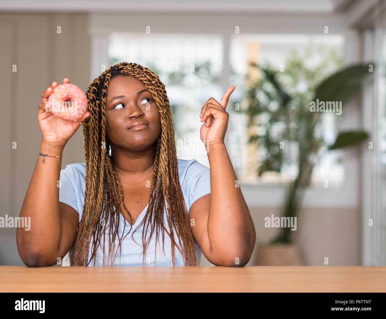 African american woman eating doughnut surprised with an idea or ...