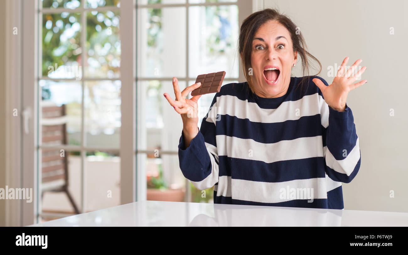 Middle aged woman eating chocolate bar very happy and excited, winner ...