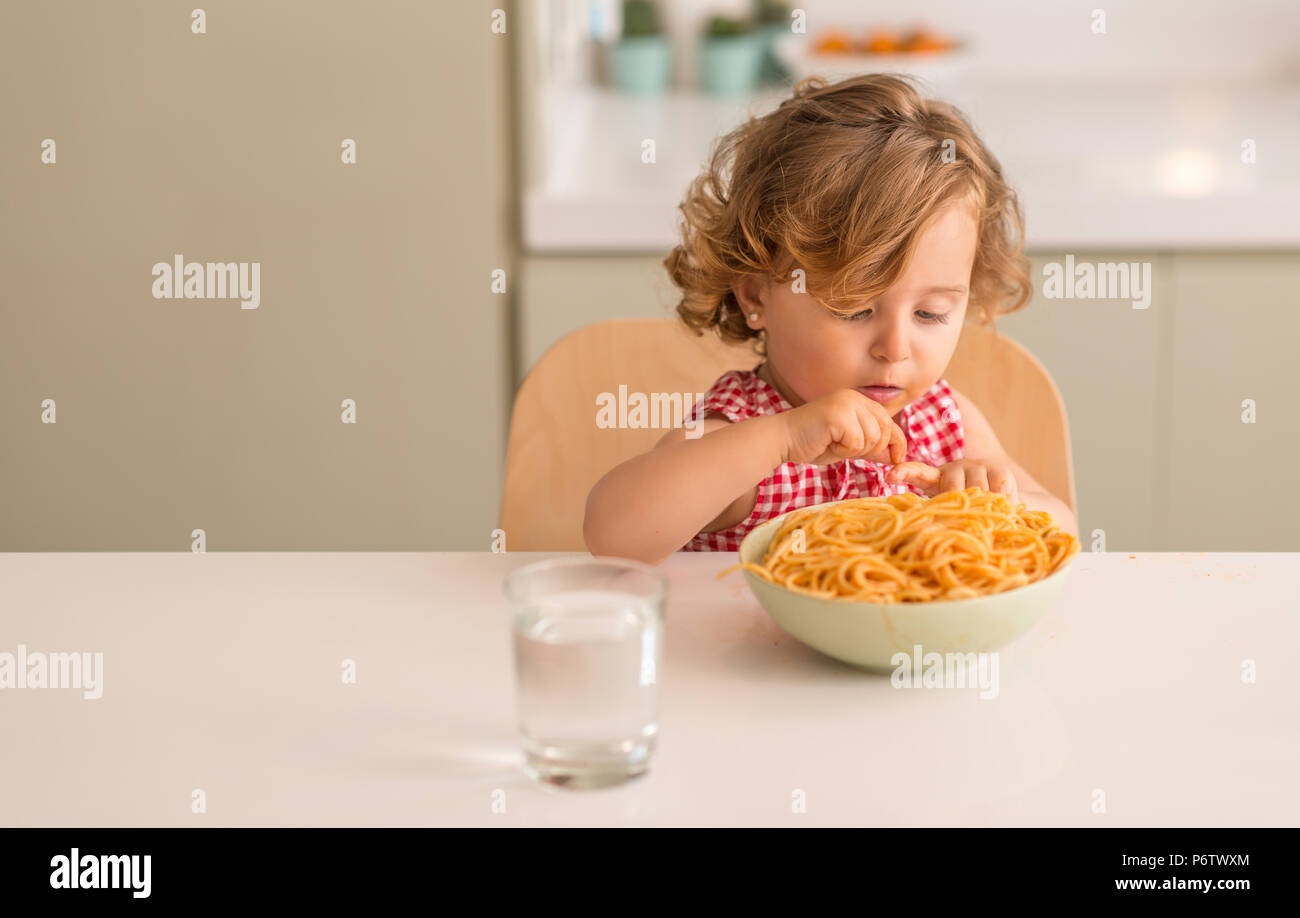 Beautiful blond child eating spaghetti with hands at home Stock Photo ...