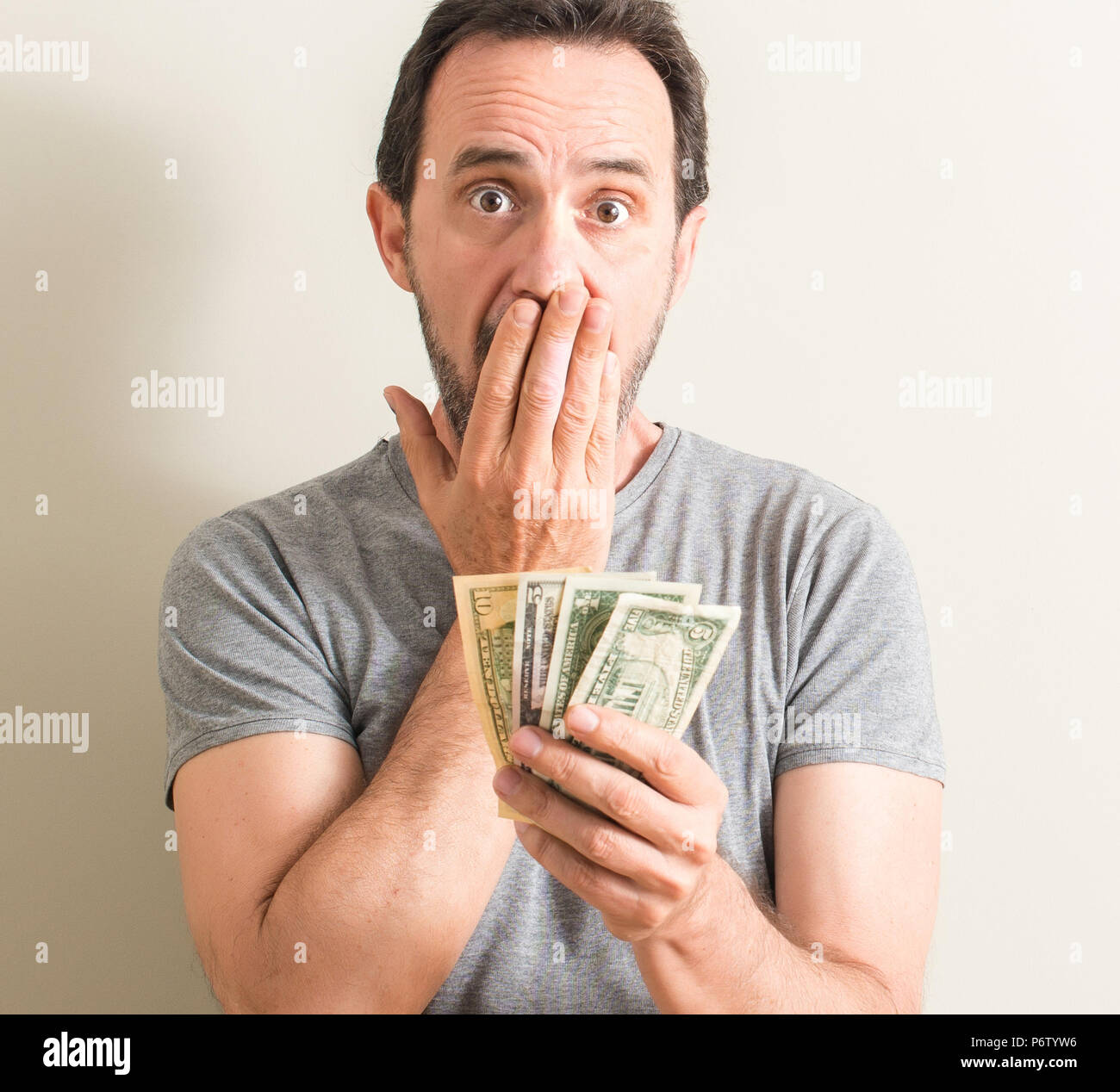 Senior man holding dollar money cover mouth with hand shocked with ...