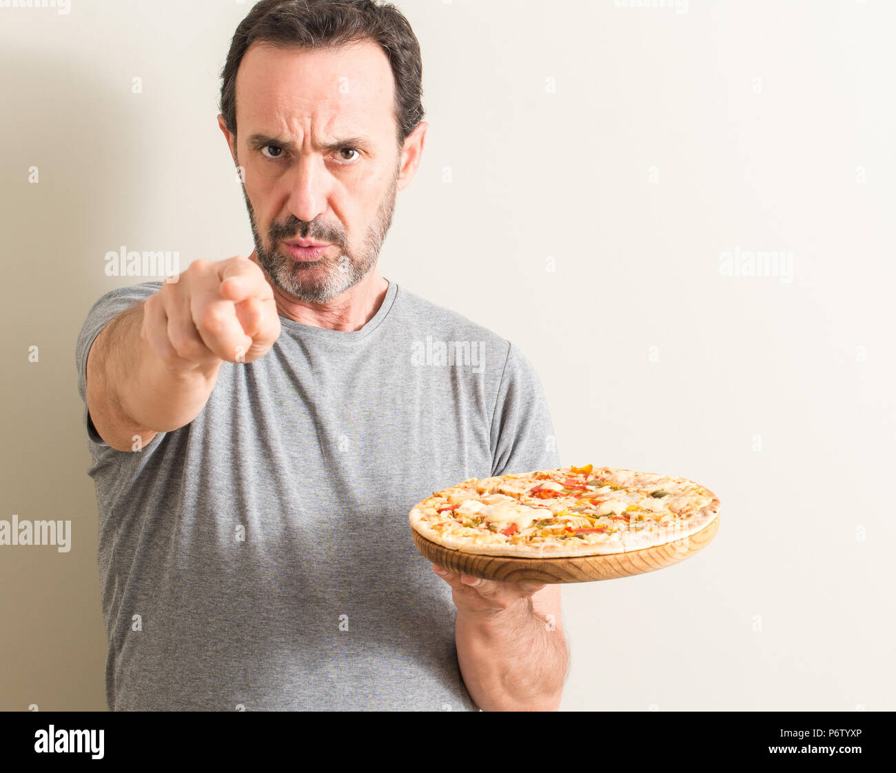 Senior man holding pizza pointing with finger to the camera and to you ...